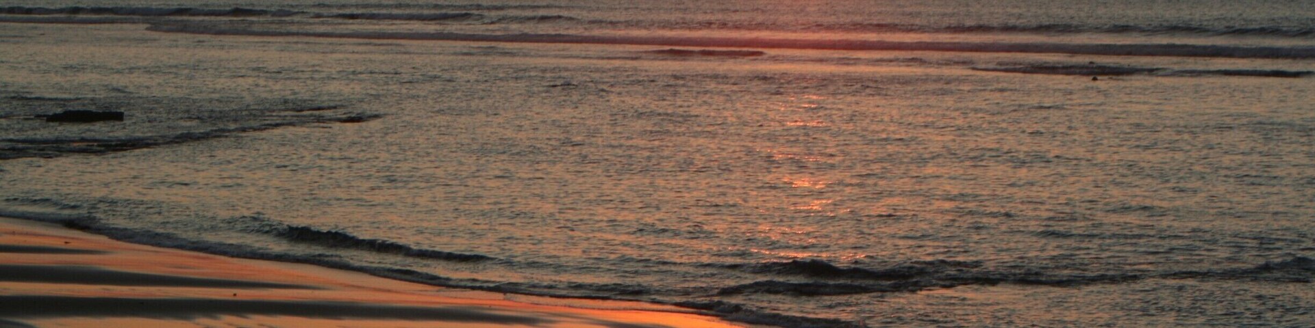Um pôr do sol sobre uma praia, com pessoas silhuetadas contra o céu.