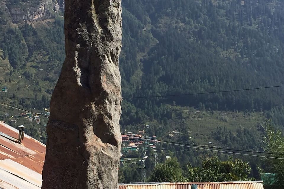 Uma grande formação rochosa em área montanhosa, com uma aldeia ao fundo.