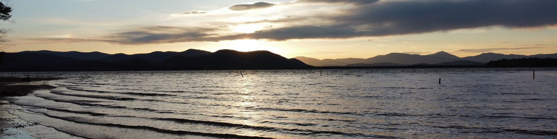Um pôr do sol sobre um lago calmo, com montanhas ao fundo.