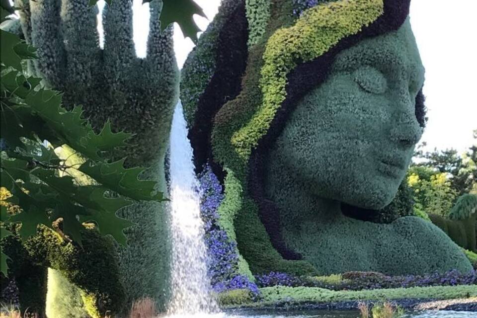 Escultura topiária grande de uma figura reclinada com uma fonte na frente.