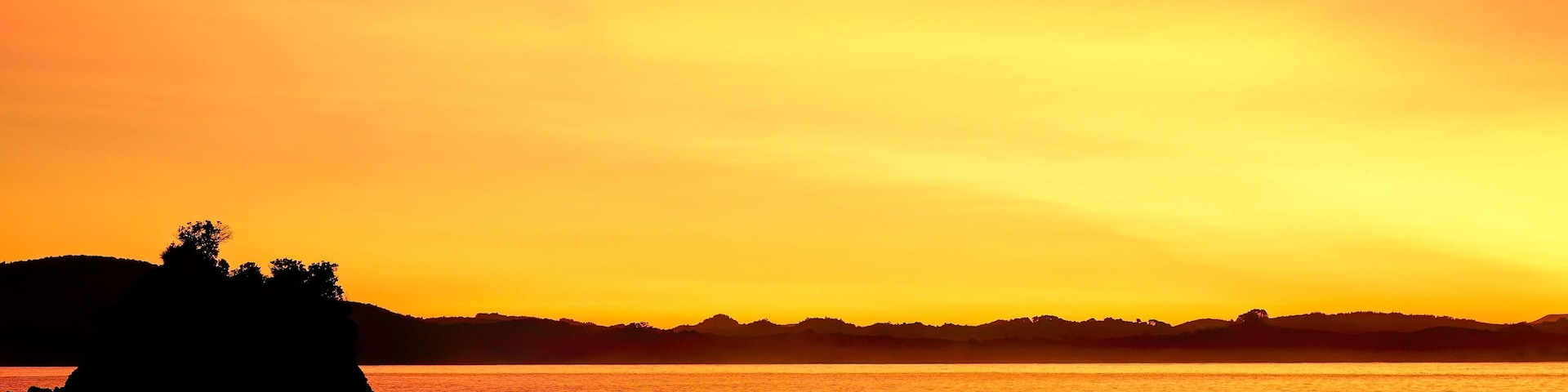 Um pôr do sol sobre uma praia com duas silhuetas de pessoas à beira-mar.