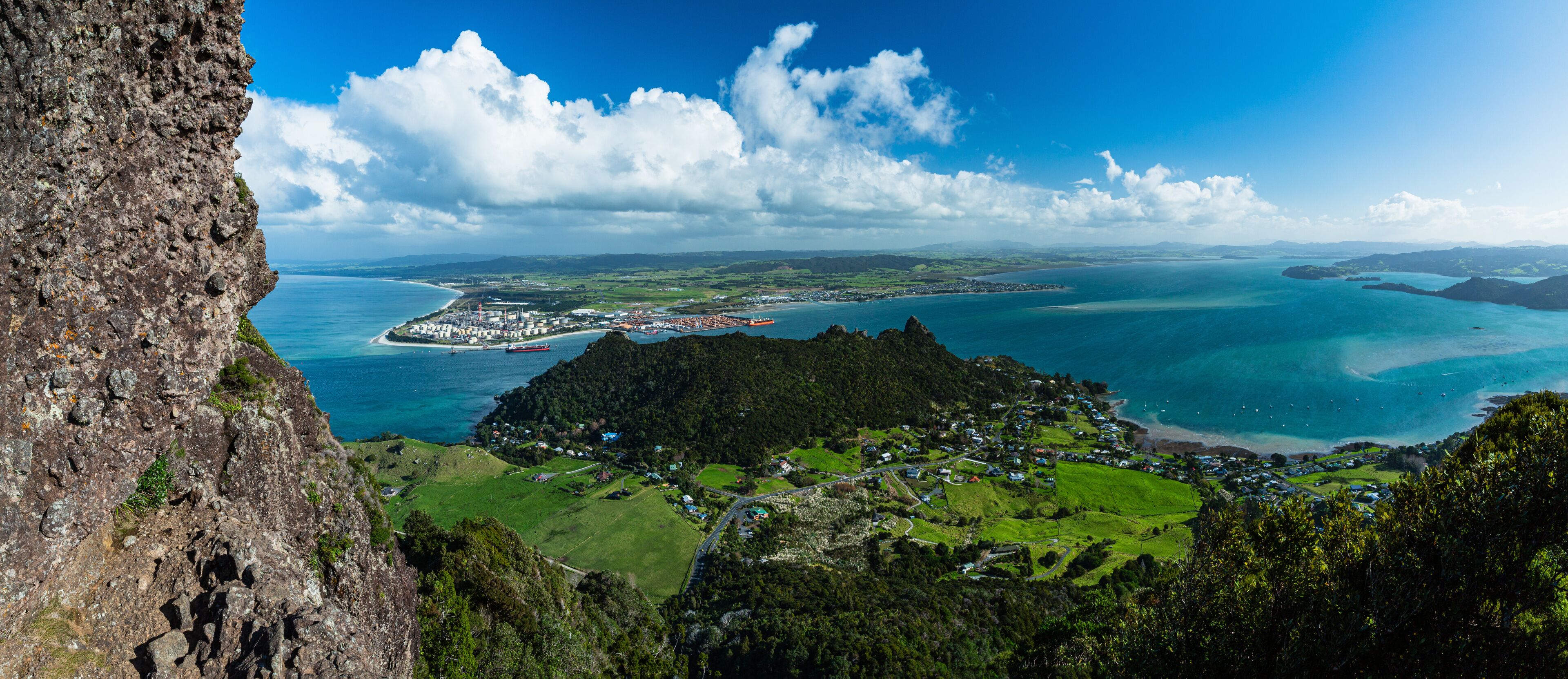 Paisagem costeira com um imponente penhasco rochoso, uma baía com uma pequena cidade e uma vasta extensão de água.