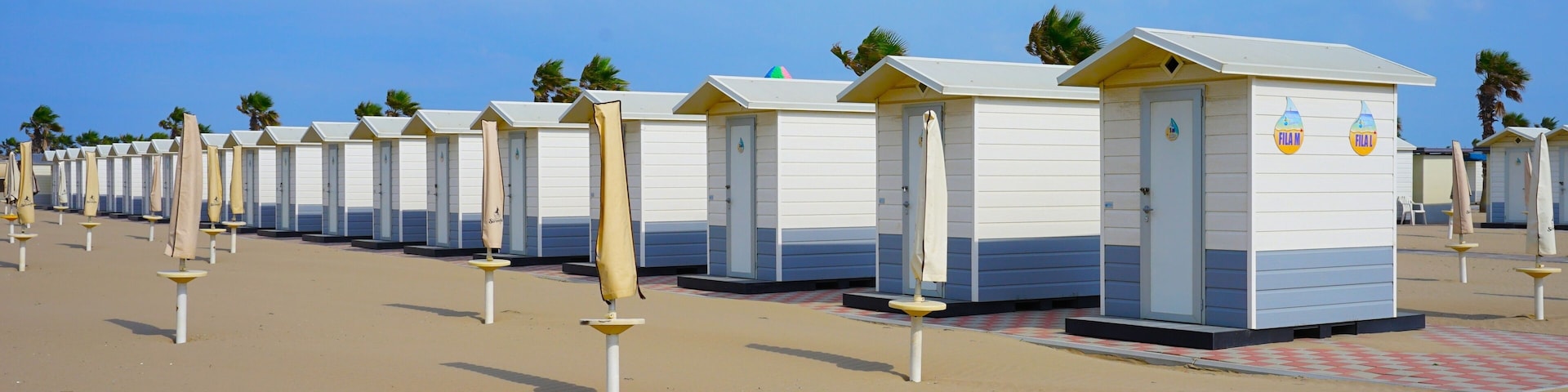 Uma fileira de cabanas de praia com guarda-sóis numa praia de areia.