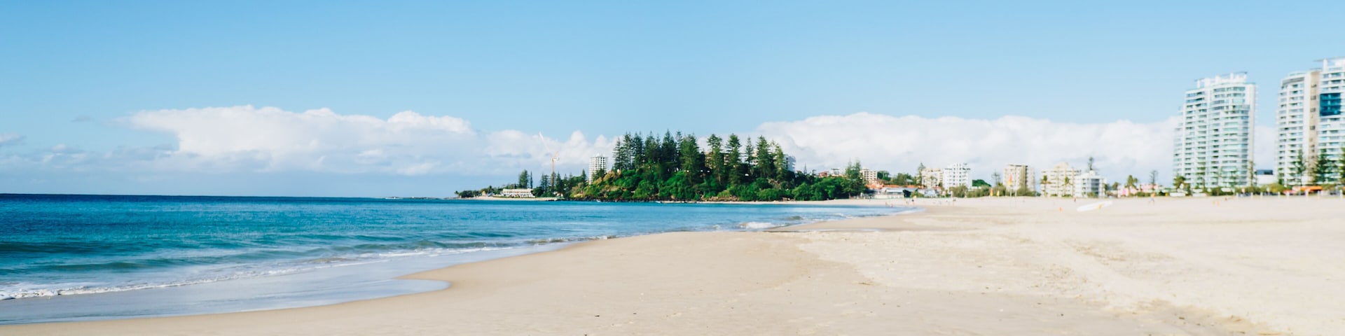 Uma praia com águas azul-claras, areal arenoso e uma ilha arborizada ao fundo.