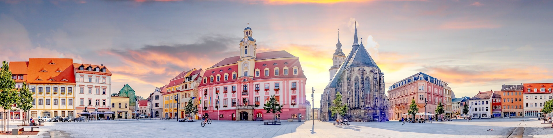 Uma praça histórica com edifícios coloridos, uma igreja imponente e um campanário.