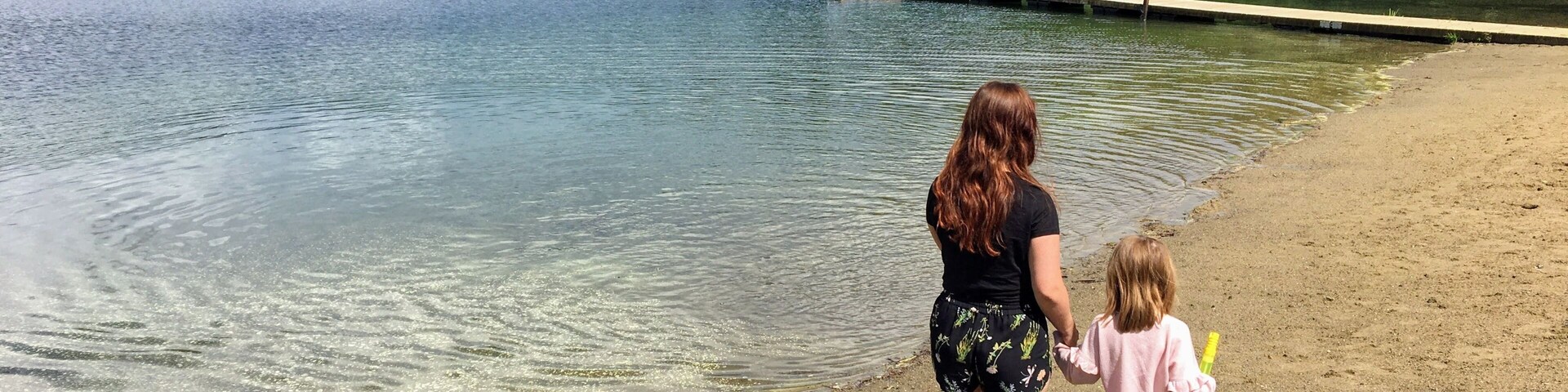 Um lago com um píer, uma encosta arborizada e um céu claro.