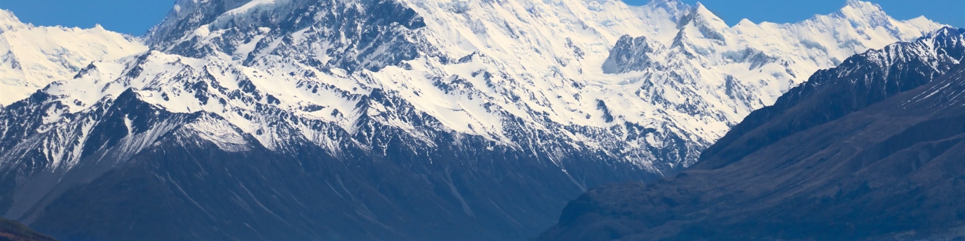 Cordilheira nevada com um lago azul-turquesa ao primeiro plano.