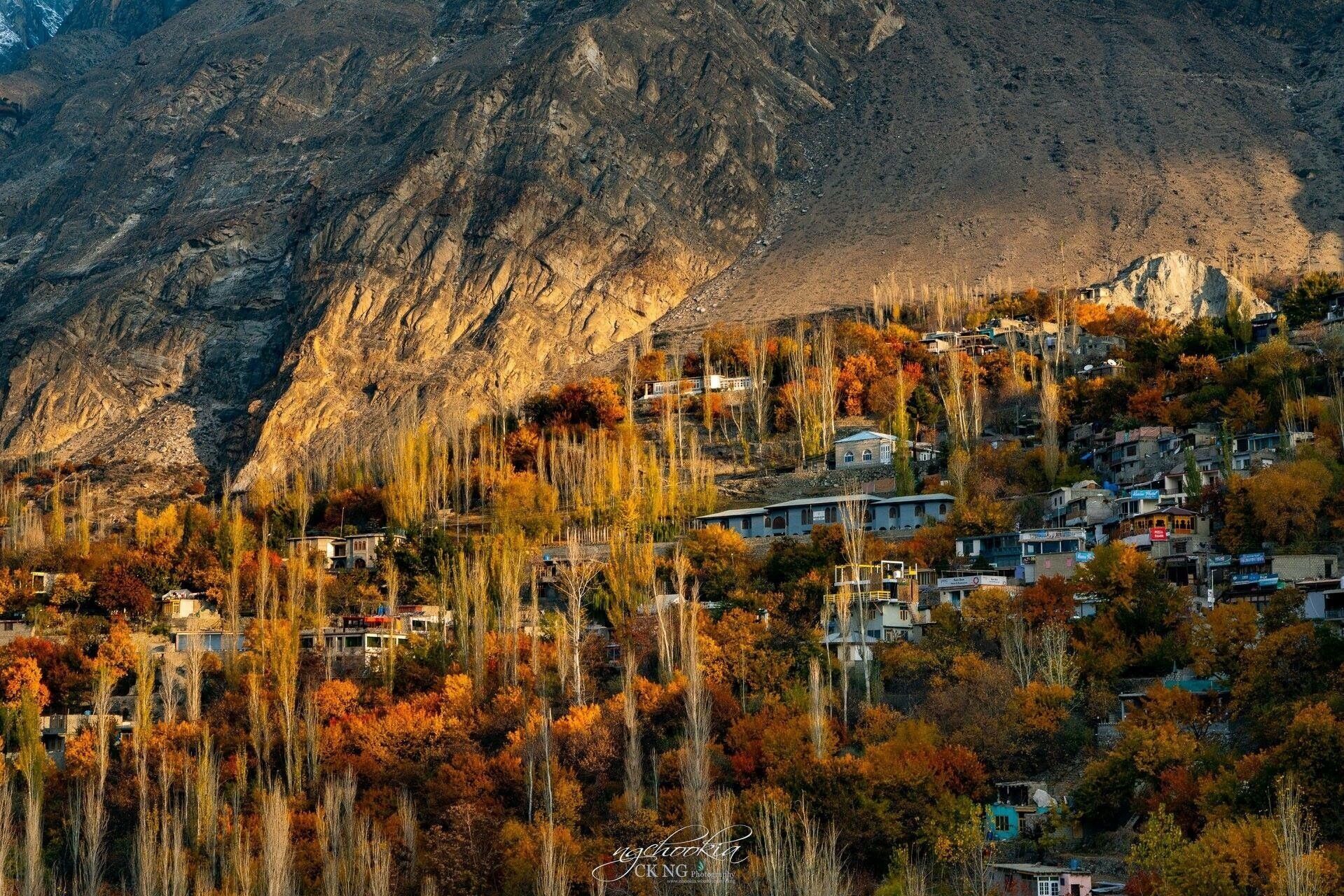 Paisagem montanhosa com árvores coloridas pelo outono e edifícios espalhados.