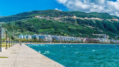 Uma cidade costeira com montanhas ao fundo, uma praia e um calçadão.