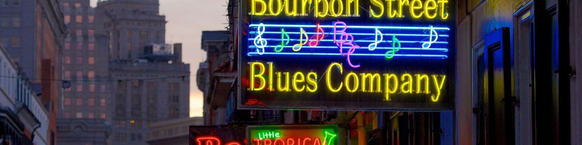 Colorful neon signs illuminate Bourbon Street's vibrant nightlife in New Orleans during twilight hours
