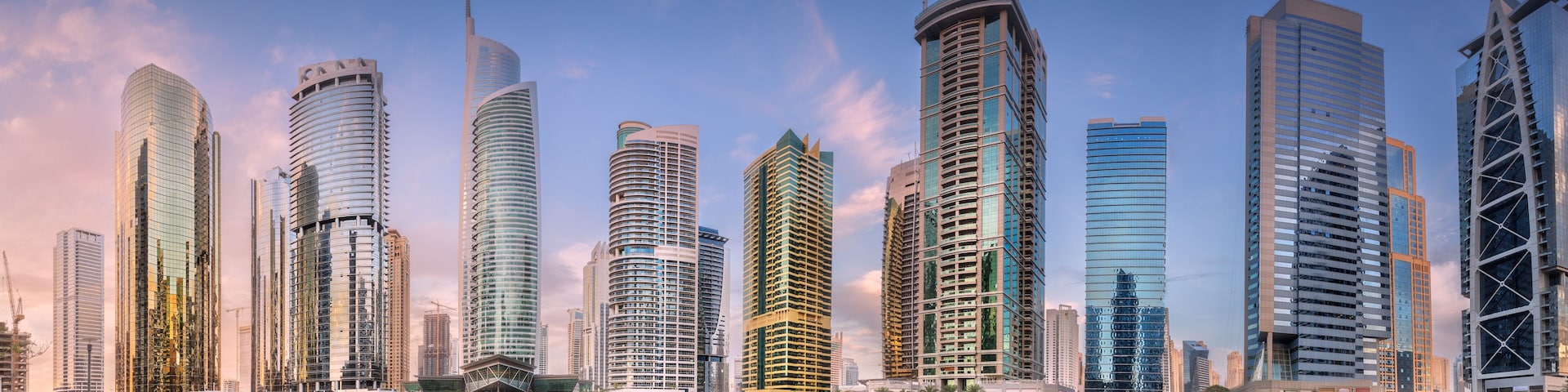 Paisagem urbana com arranha-céus modernos, um corpo d'água tranquilo refletindo os edifícios e um céu claro.
