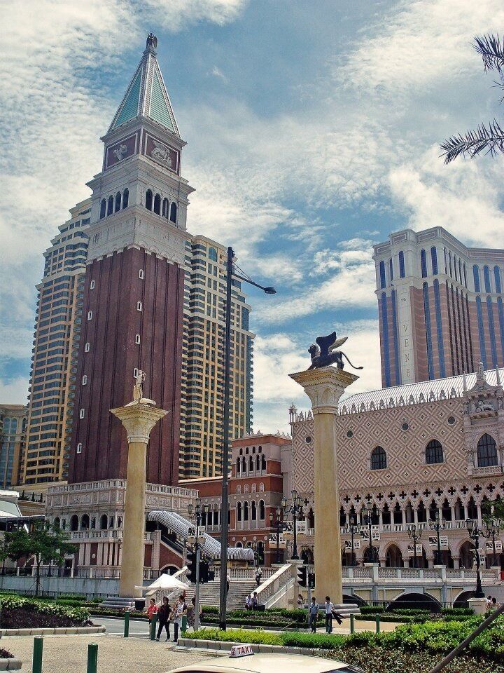 Um edifício histórico com torre de relógio, um arranha-céu moderno e duas colunas ornamentadas com estátuas.