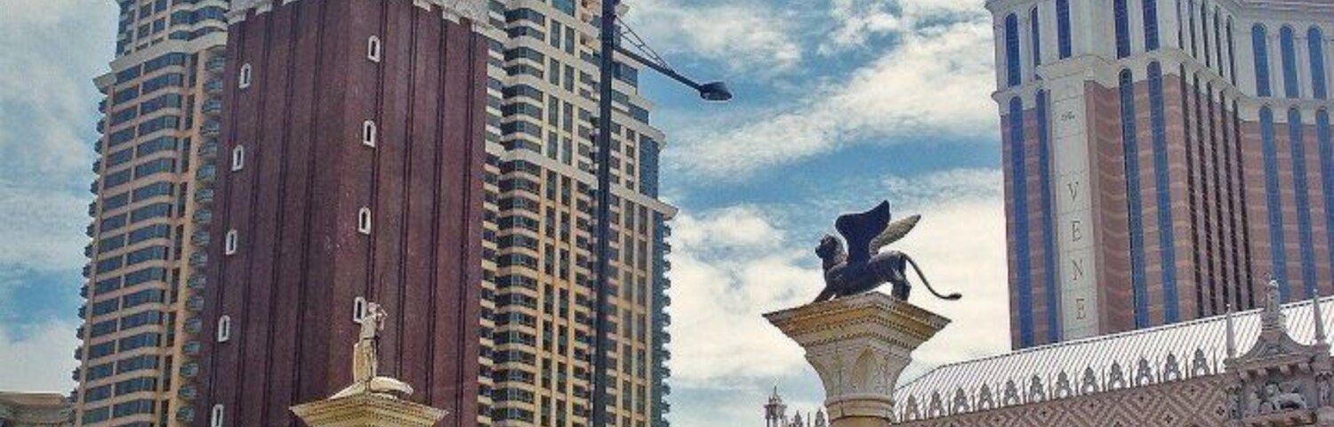 Um edifício histórico com torre de relógio, um arranha-céu moderno e duas colunas ornamentadas com estátuas.