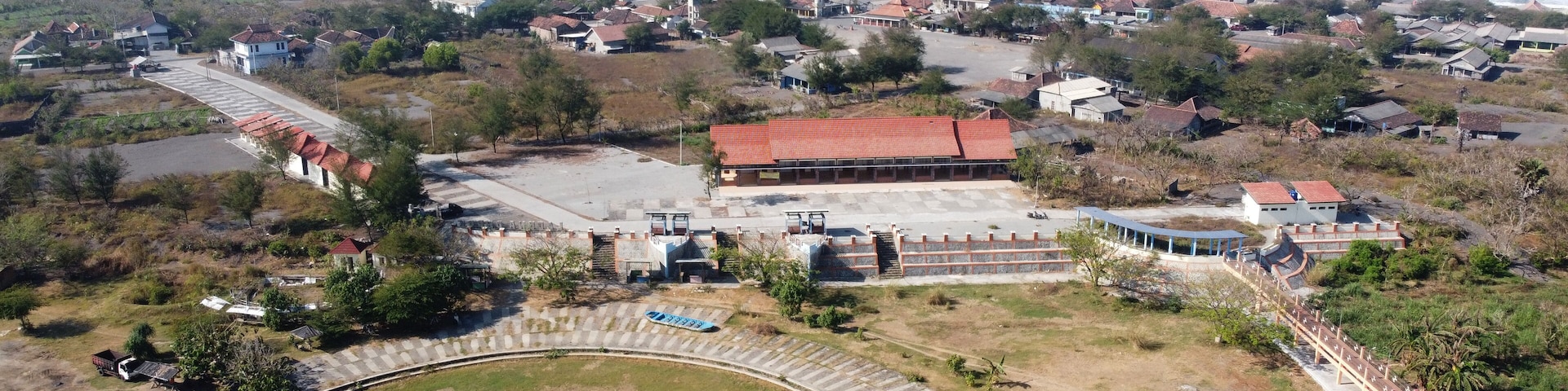 Vista aérea de uma cidade costeira com praia, farol e uma grande praça aberta.