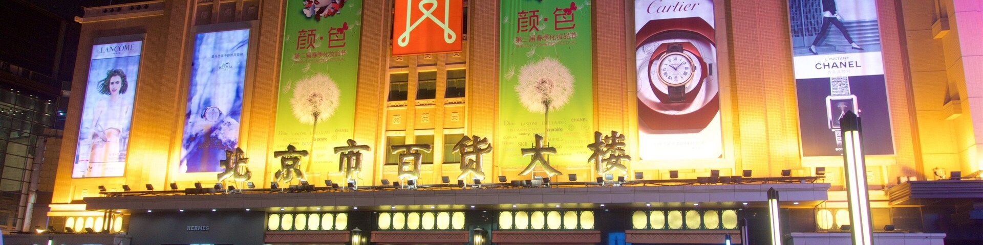 Um edifício bem iluminado com grandes anúncios de marcas como Lancome, Chanel e Cartier.