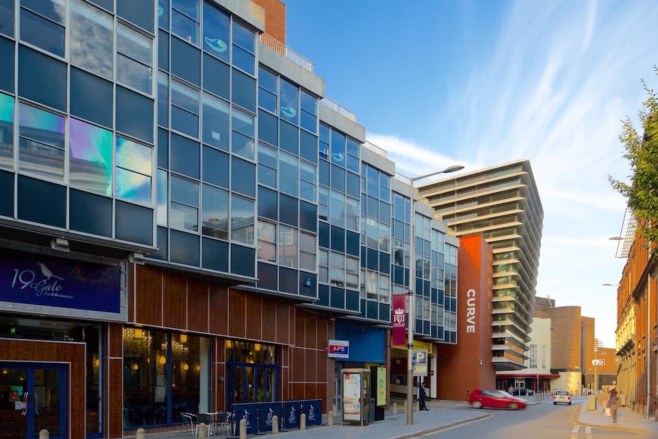Uma rua urbana moderna com uma variedade de edifícios comerciais, incluindo um restaurante chamado '19 Gate' e um edifício com a placa 'CURVE'.