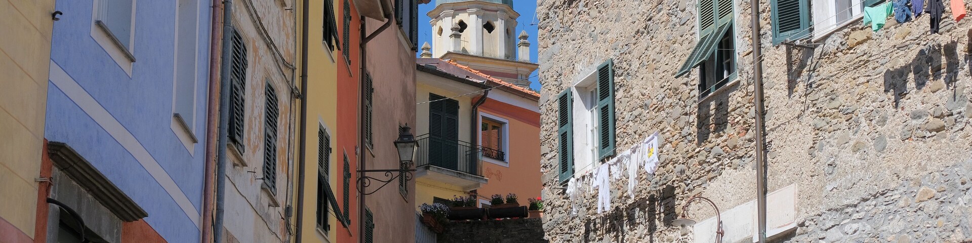 Uma rua estreita com edifícios coloridos, uma parede de pedra e um campanário.