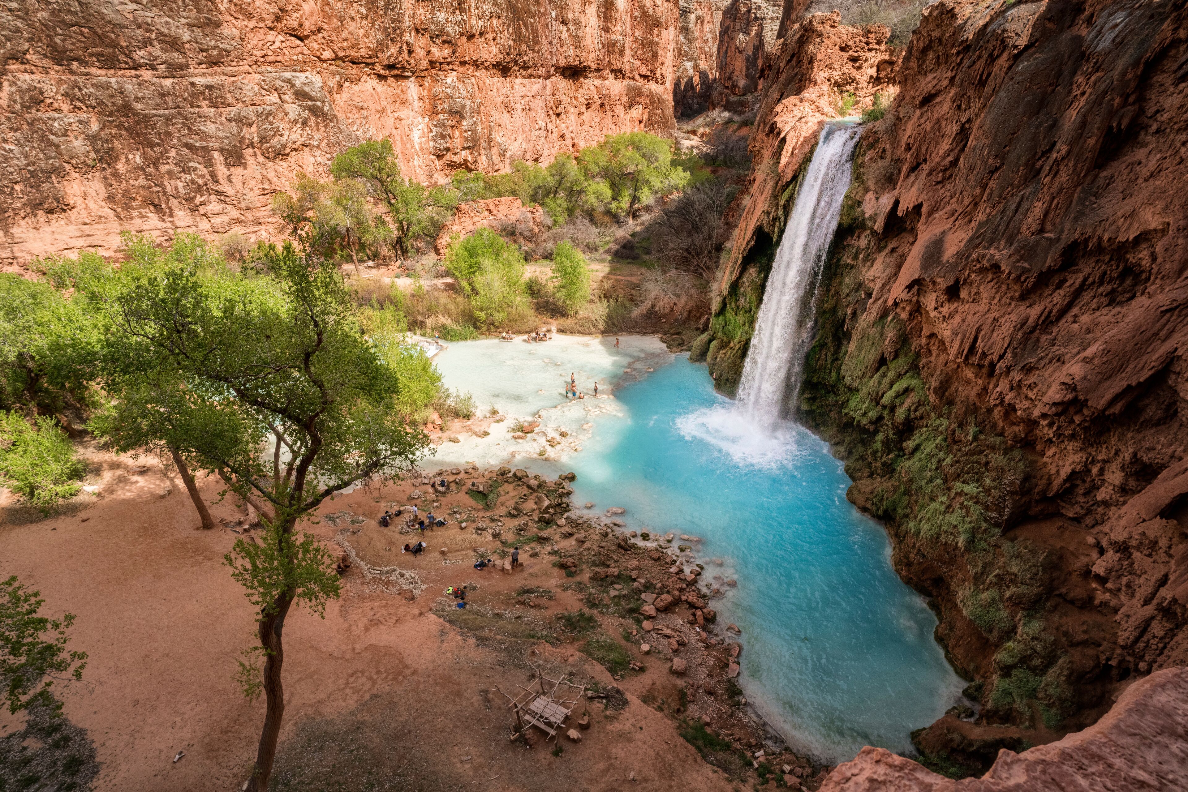 Uma cascata deságua em uma piscina turquesa, rodeada por penhascos rochosos e vegetação rasteira.