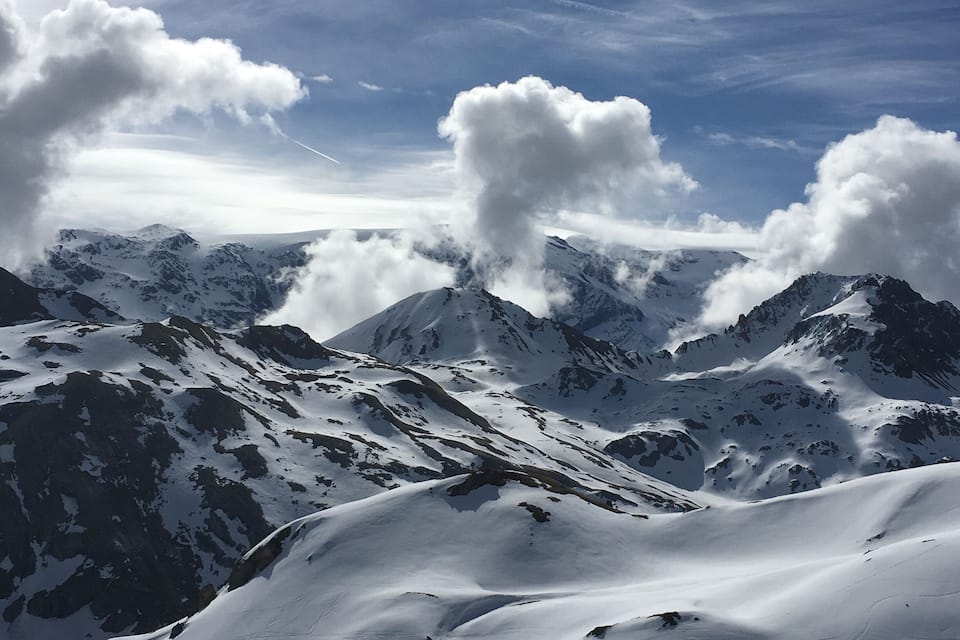 Cordilheira nevada com picos imponentes e nuvens.