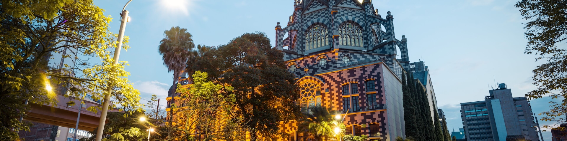 Um edifício histórico com arquitetura elaborada e uma grande cúpula, rodeado por uma praça com pessoas e árvores.