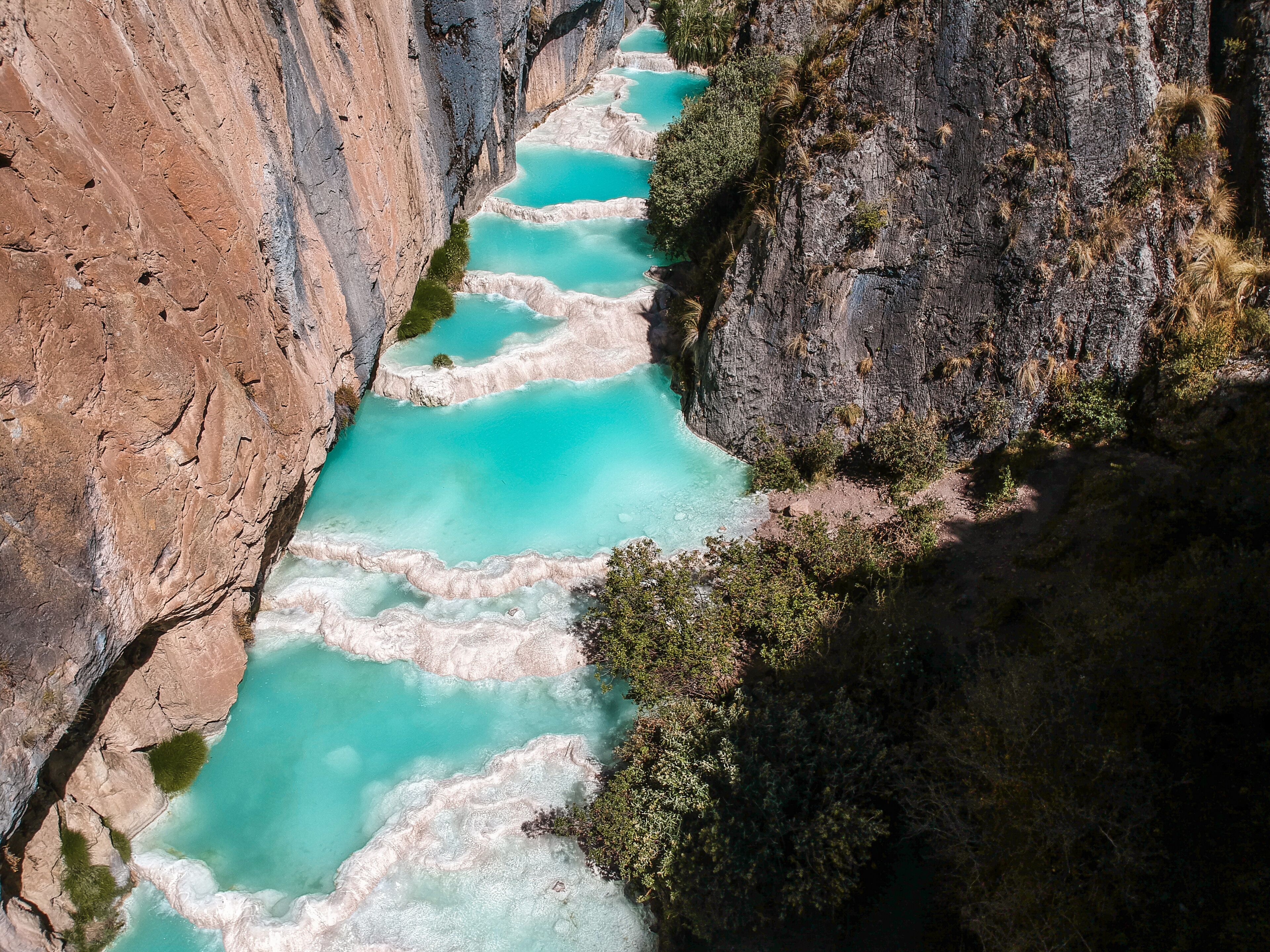 Um rio azul-turquesa serpenteando por um cânion com penhascos rochosos e vegetação rasteira.