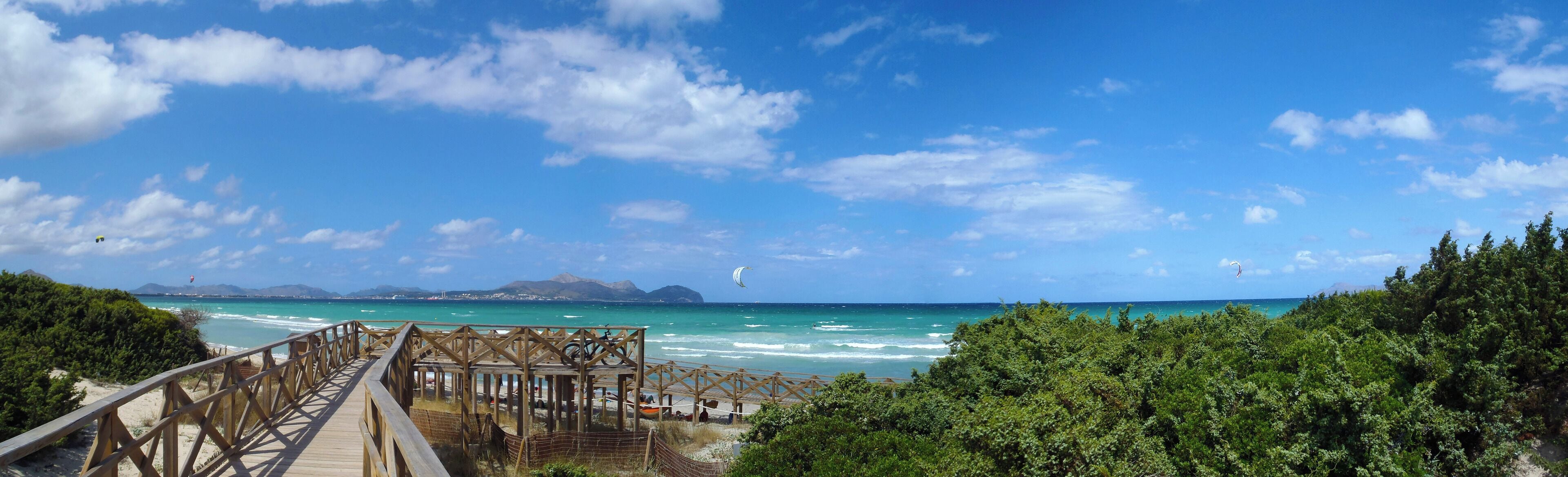Uma passarela de madeira que leva a uma praia com águas azul-turquesa e céu claro.
