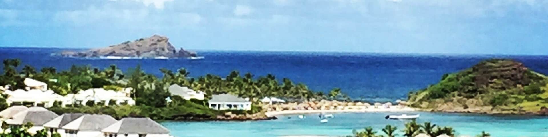 Uma área costeira com edifícios, praia e uma pequena ilha ao longe.
