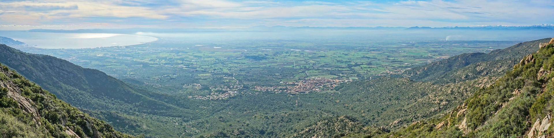 Paisagem montanhosa com um vale, uma massa de água ao longe e uma pequena cidade.