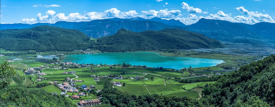 Paisagem montanhosa com um lago, vinhedos e uma pequena aldeia.