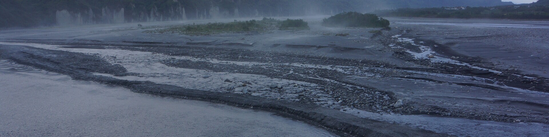 Um rio com margens rochosas e montanhas ao longe, sob um céu nublado.
