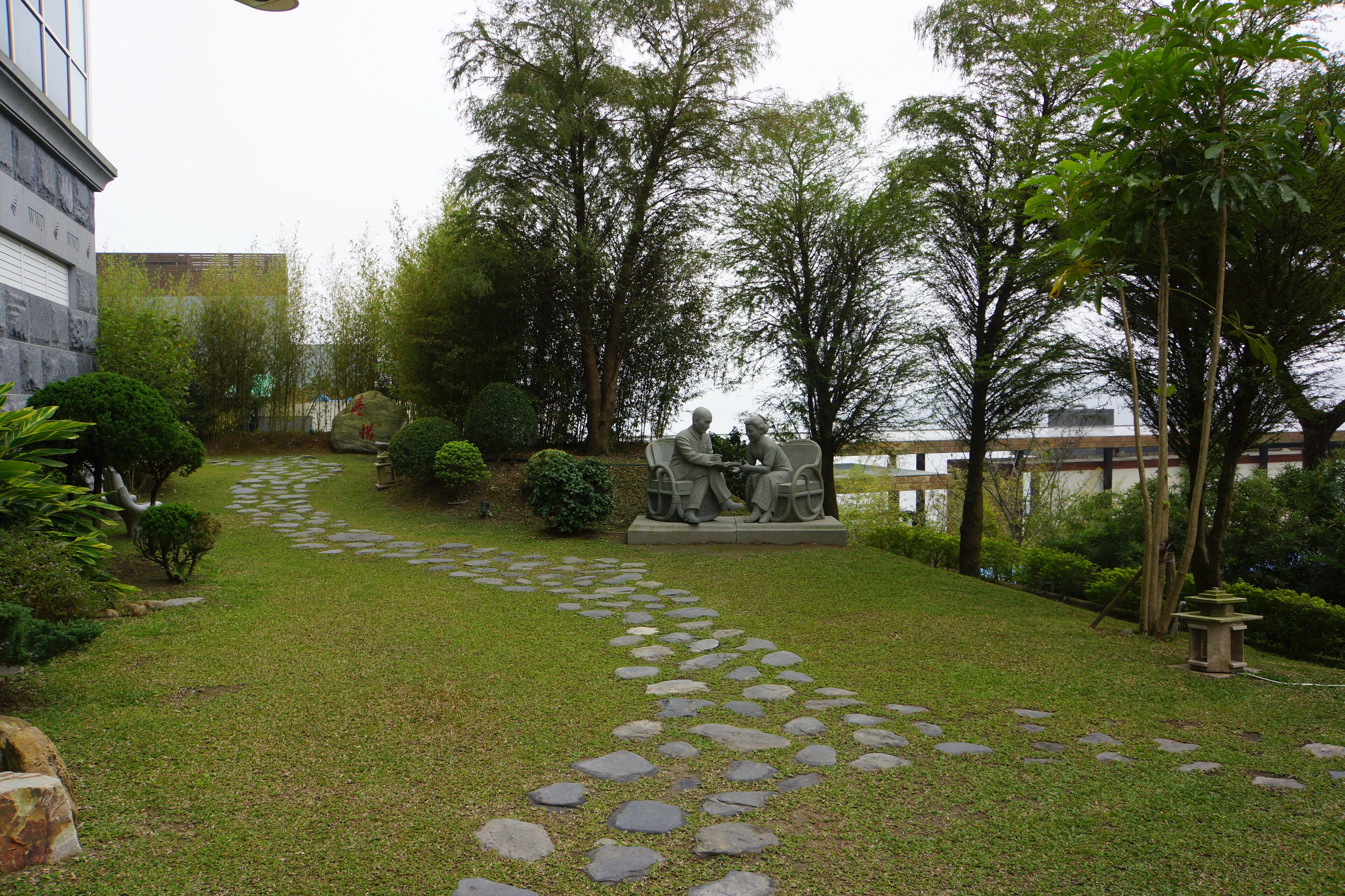 Um jardim com caminho de pedra, estátuas e vegetação exuberante.
