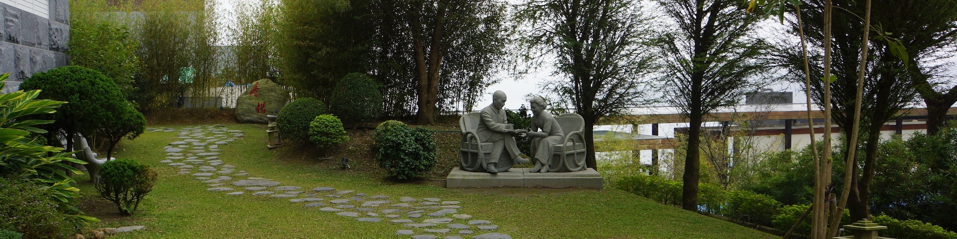 Um jardim com caminho de pedra, estátuas e vegetação exuberante.