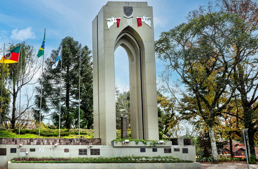 Um monumento alto com arcos, rodeado por árvores e bandeiras.