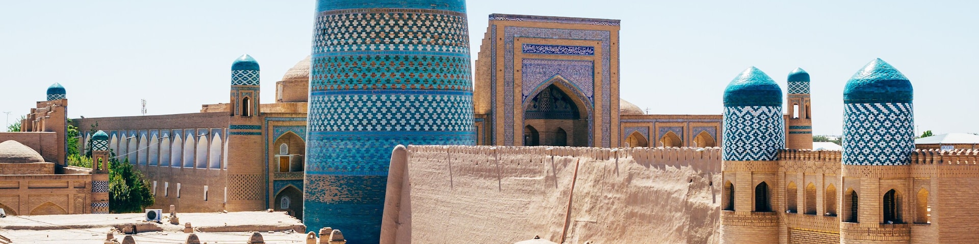 Paisagem urbana histórica com arquitetura tradicional, incluindo um minarete azul com telhas destacadas e um edifício grande com padrões elaborados.