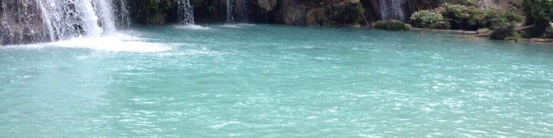 Uma cascata deságua numa piscina azul-turquesa, rodeada por vegetação exuberante.