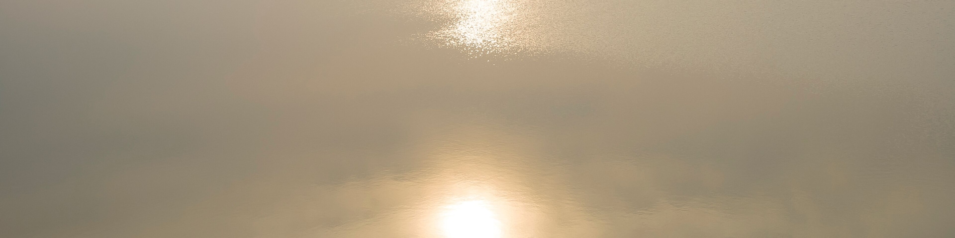 Uma praia com ondas calmas e um reflexo claro do sol na água.