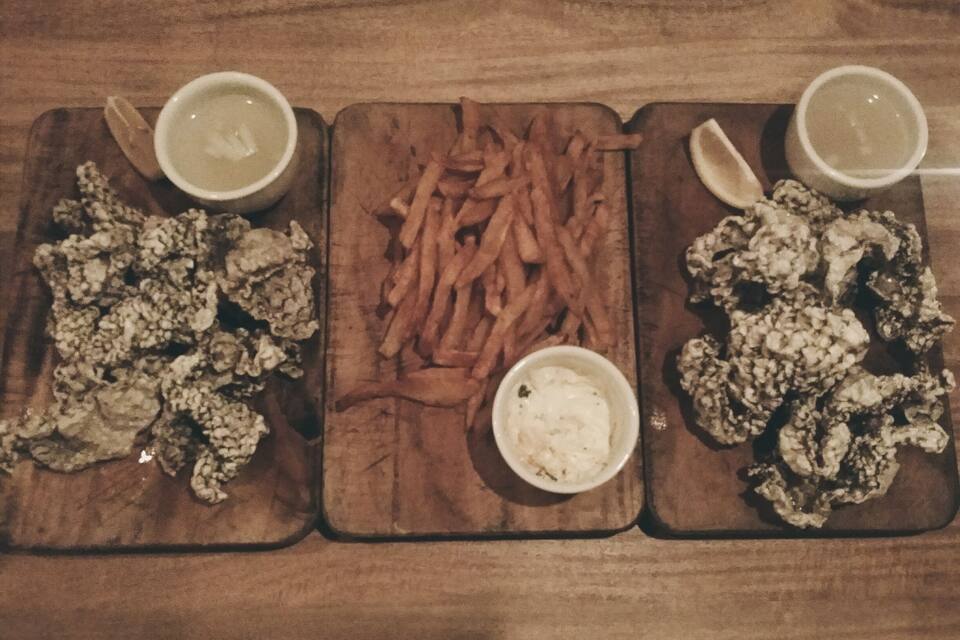 Uma mesa de madeira com duas porções de frango frito, um prato de batatas fritas e dois pequenos copos de molho.