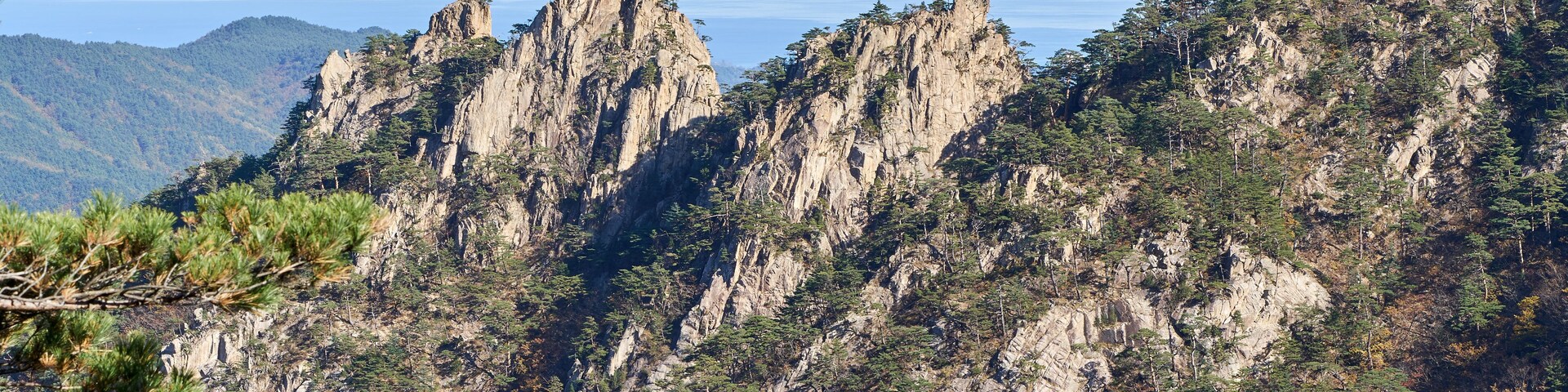 Paisagem montanhosa com picos rochosos imponentes e densa vegetação.
