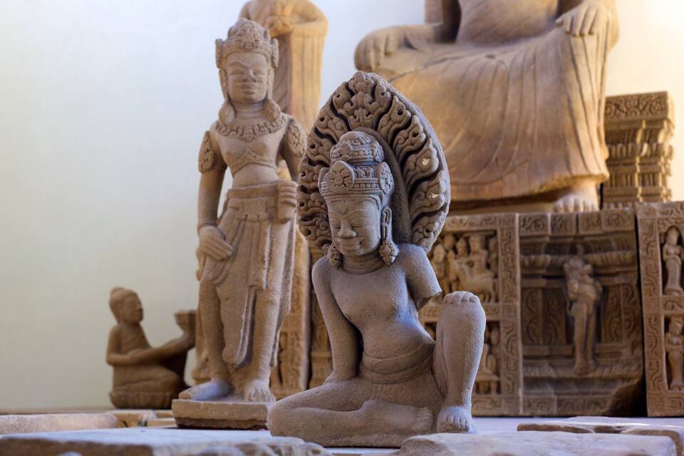 Um conjunto de estátuas de pedra, incluindo uma figura sentada e outra de pé com um headdress.