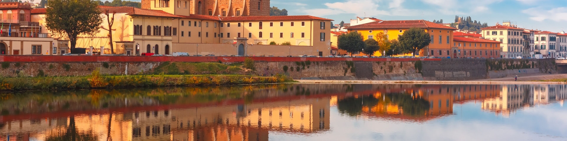 Um rio calmo refletindo edifícios históricos, incluindo uma igreja notável com cúpula e campanário.