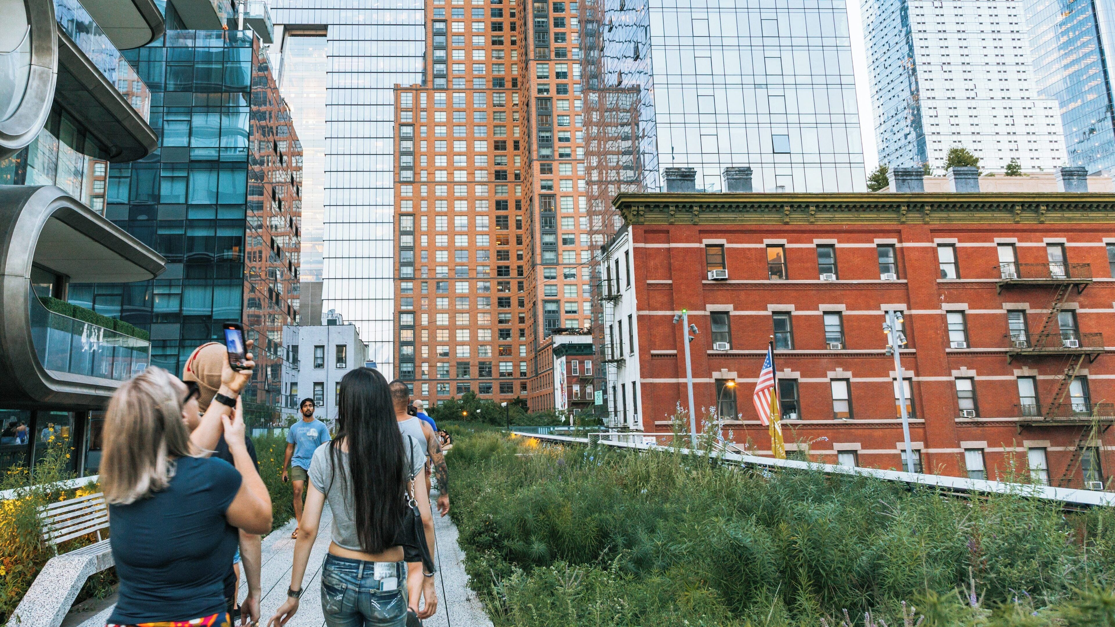 Visitors explore The High Line Park in Manhattan, enjoying urban greenery and modern architecture on a sunny day