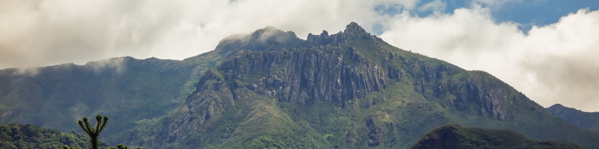 Montanha com vegetação verde densa e céu claro com nuvens.