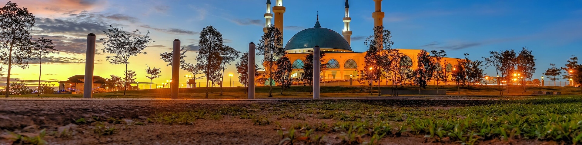 Uma mesquita com uma cúpula grande e quatro minaretes, cercada por árvores e uma superfície aquática refletora.