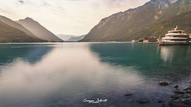 Um lago calmo com um barco grande, montanhas e céu claro.