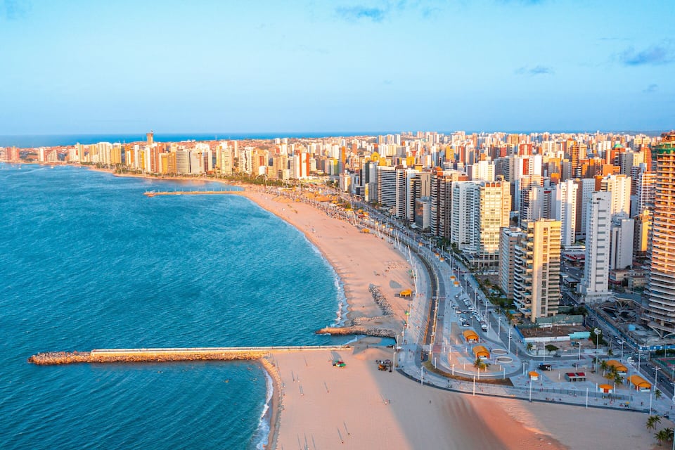 Paisagem costeira com praia, edifícios altos e um cais.
