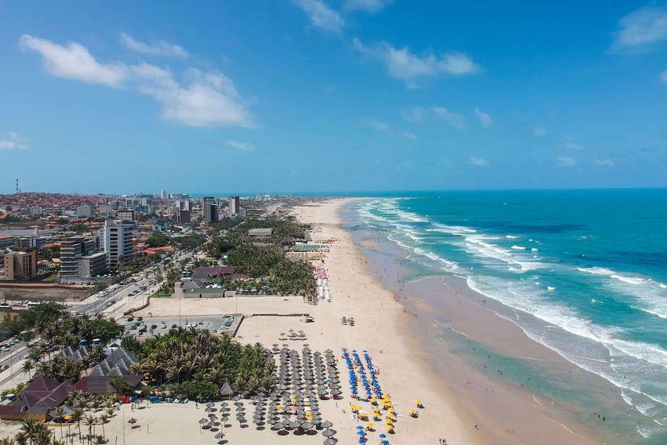 Paisagem costeira com uma extensa praia, céu azul límpido e ondas do oceano.