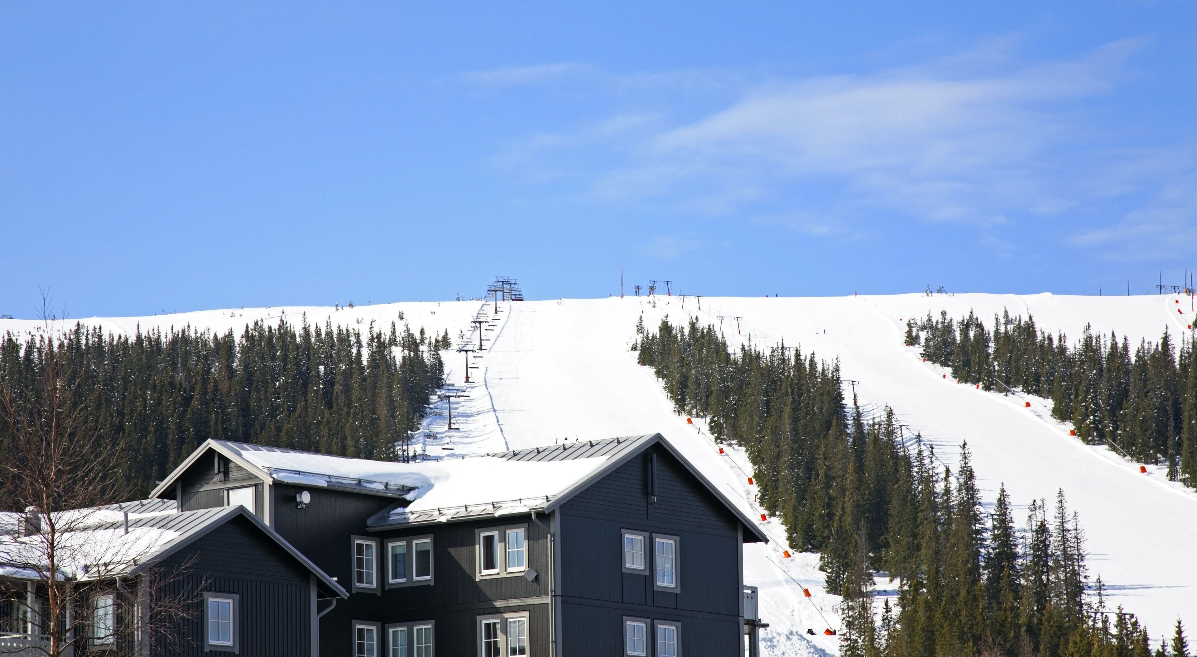 Montanha coberta de neve com teleféricos, pista de esqui e um edifício com telhado escuro.