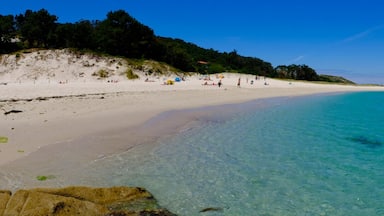 Uma praia com águas turquesa cristalinas, areal arenoso e afloramentos rochosos.