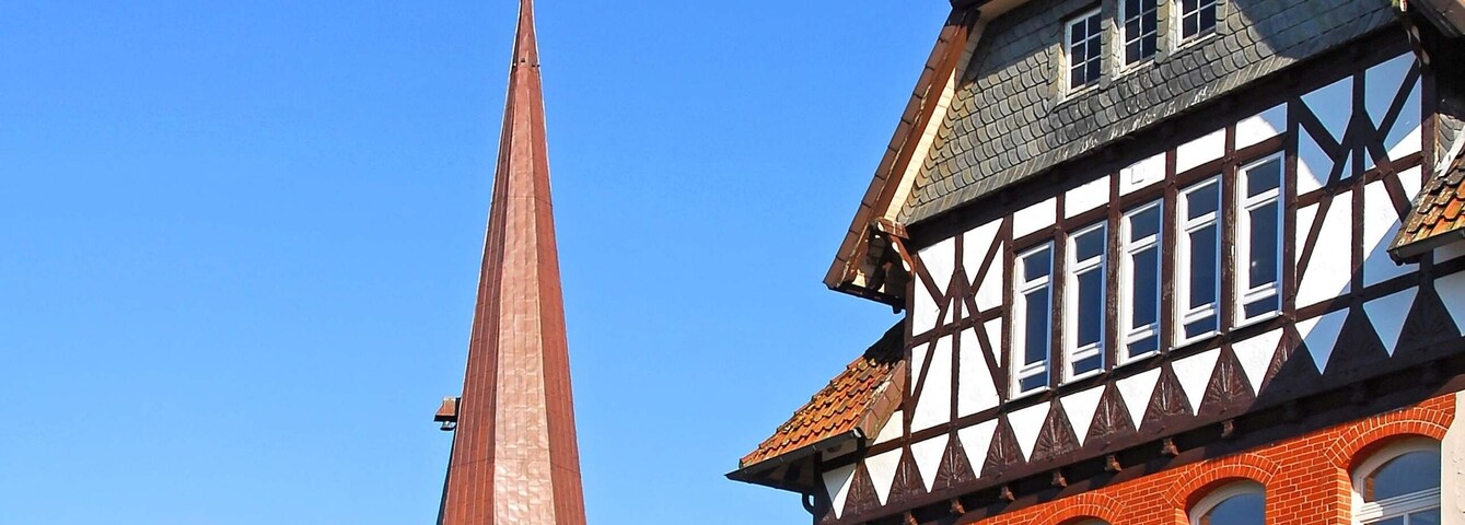 Uma igreja com uma torre alta, um edifício tradicional em enxaimel e um ponto de ônibus.