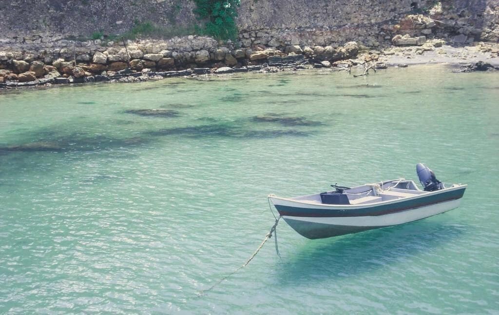 Um pequeno barco ancorado em águas turquesa cristalinas, com uma costa rochosa ao fundo.